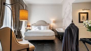 Quarto de hotel com cama, poltrona, luminária, banheira e roupão pendurado em um suporte.