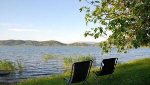 Duas cadeiras dobráveis pretas perto de um lago, com margens gramadas e um galho de árvore acima.