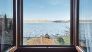 Visão pela janela de um lago com barcos, área gramada e colinas ao longe.