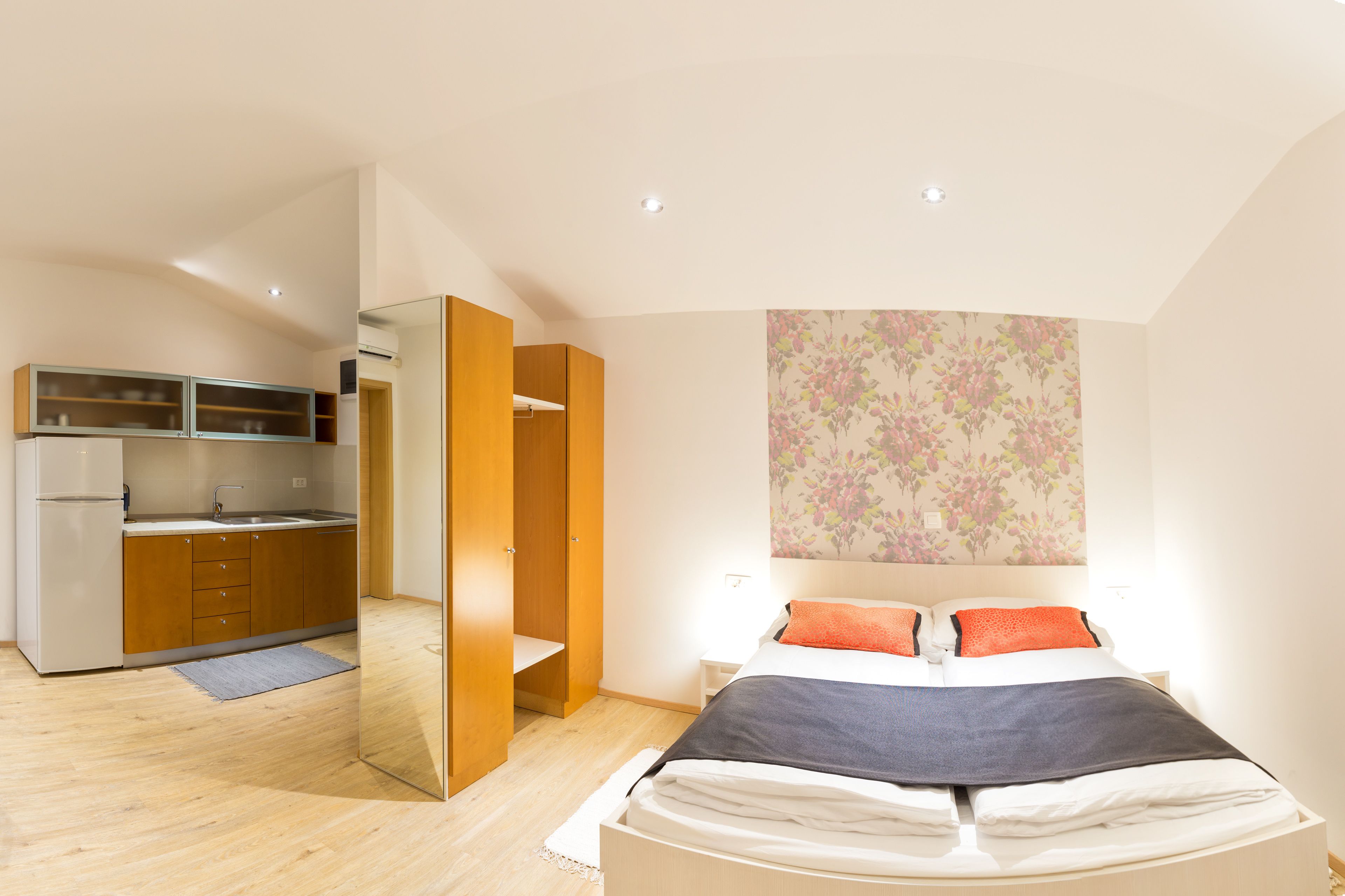 Quarto moderno com cama, mesa de cabeceira, espelho, guarda-roupa e cozinha.