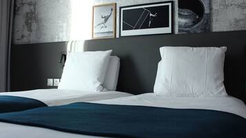 Quarto de hotel com uma cama grande, duas almofadas brancas, cabeceira escura e fotografias de esportes emolduradas na parede.