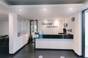 Uma área de recepção com uma placa que diz "iSilver Less is more", um balcão de atendimento, um relógio e uma tela de televisão.