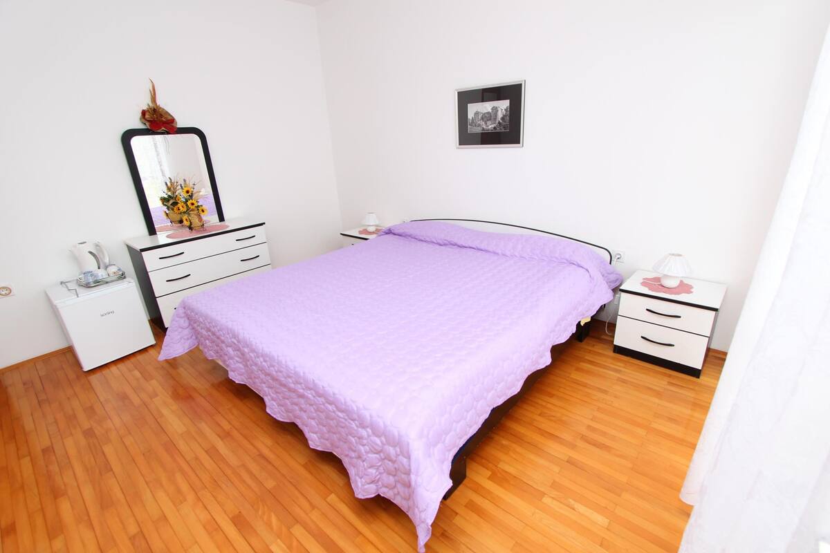 Quarto com cama, penteadeira, mesa de cabeceira, espelho e um quadro na parede.