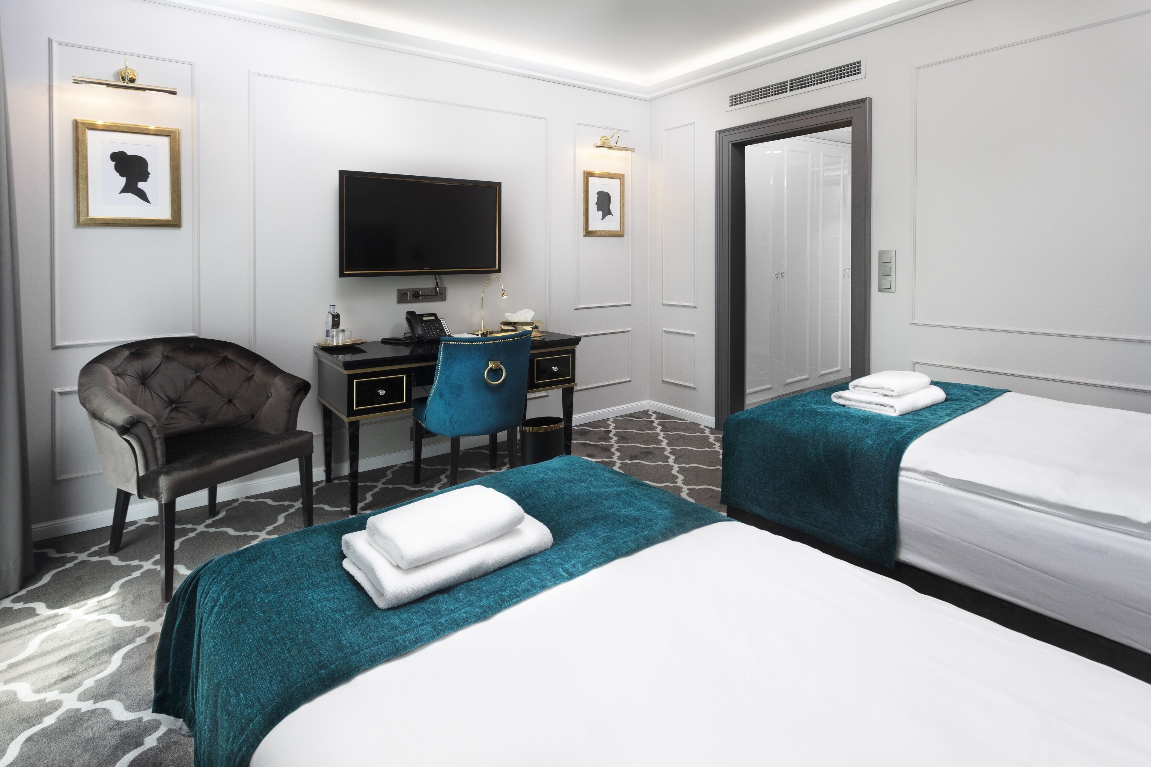 Quarto de hotel com duas camas, uma escrivaninha, uma cadeira, uma televisão e uma porta.