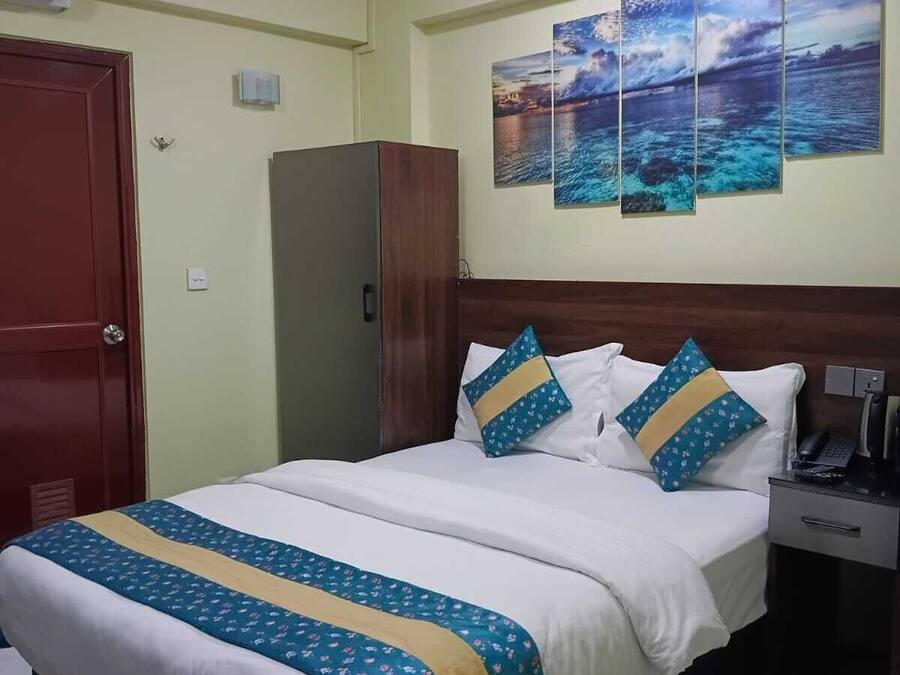 Uma cama bem arrumada com colcha azul e amarela, cabeceira de madeira e mesa de cabeceira com telefone e abajur.