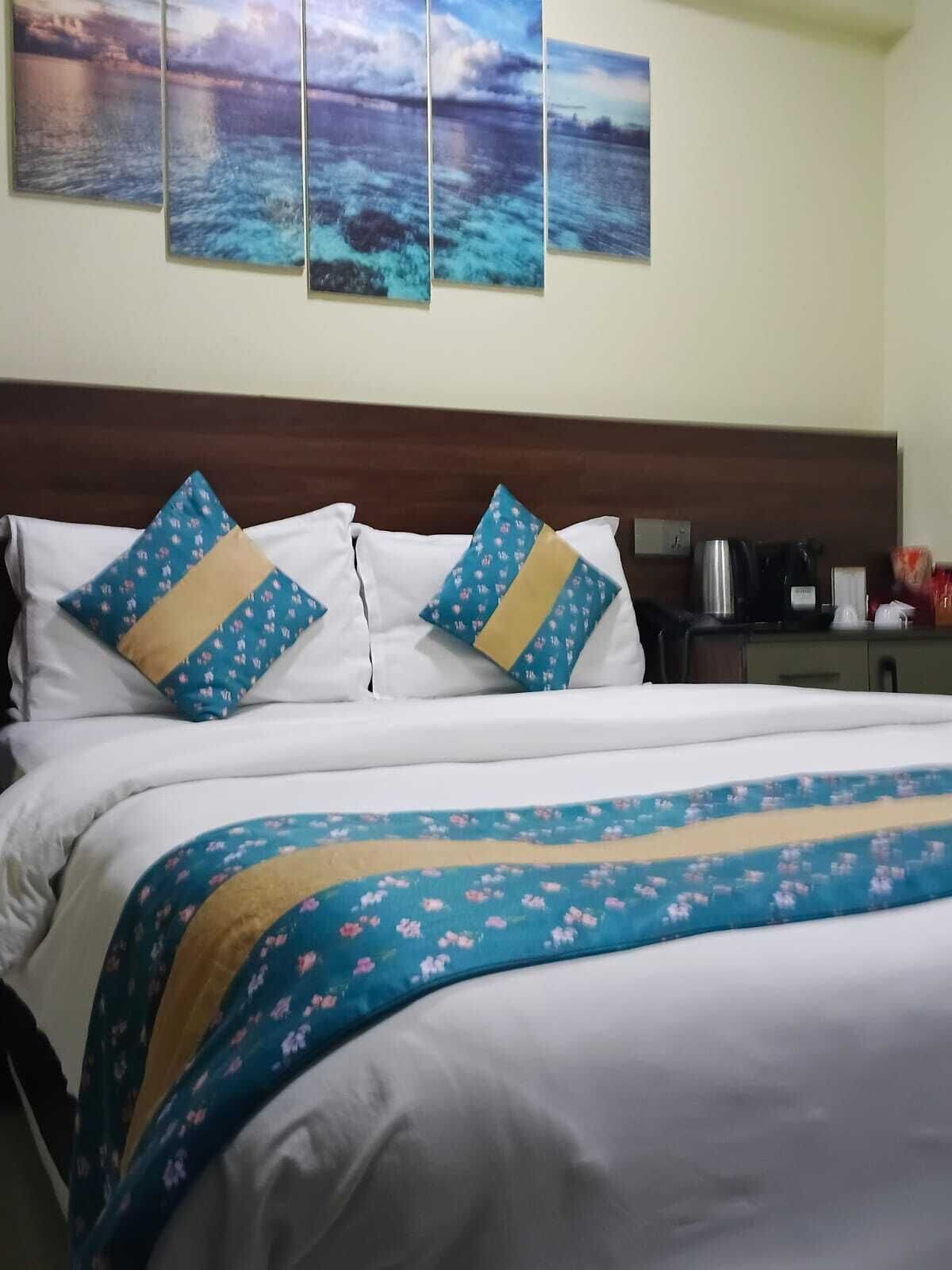 Uma cama bem arrumada com roupa de cama estampada em florais, cabeceira de madeira e mesa de cabeceira com cafeteira e outros objetos.
