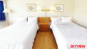Quarto de hotel com duas camas de solteiro, uma mesa de cabeceira de madeira, uma luminária e duas luminárias fixadas na parede.