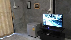 Quarto com televisão sobre suporte preto, uma pequena geladeira e piso ladrilhado.