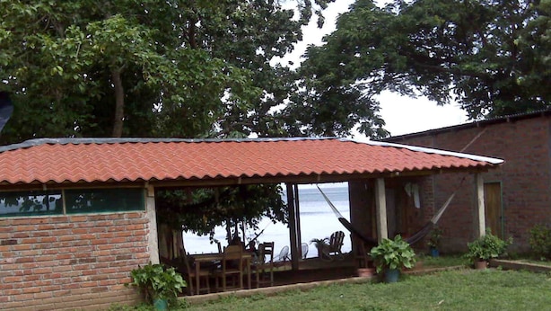 Uma casa de tijolos com telhado de telhas vermelhas, um alpendre com móveis de exterior e vista para a água.