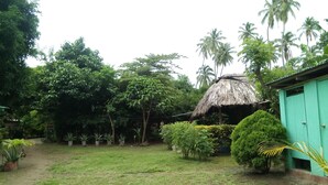 Um jardim exuberante com uma construção de telhado de palha, rodeado por diversas plantas e árvores.