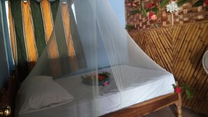 Uma cama com mosquiteiro, cabeceira de madeira e parede com padrão e flores tecidas.