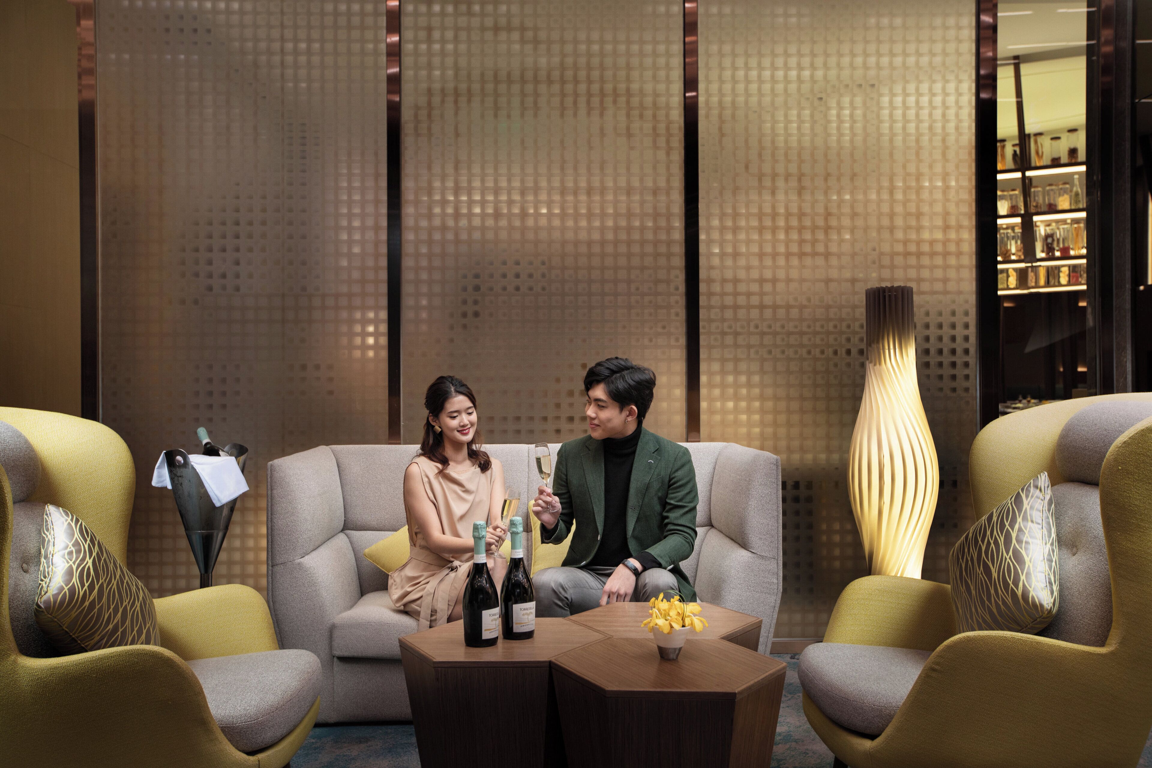 Um interior moderno com um sofá, duas poltronas, uma mesa de centro com garrafas de vinho e um vaso decorativo.