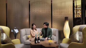 Um interior moderno com um sofá, duas poltronas, uma mesa de centro com garrafas de vinho e um vaso decorativo.