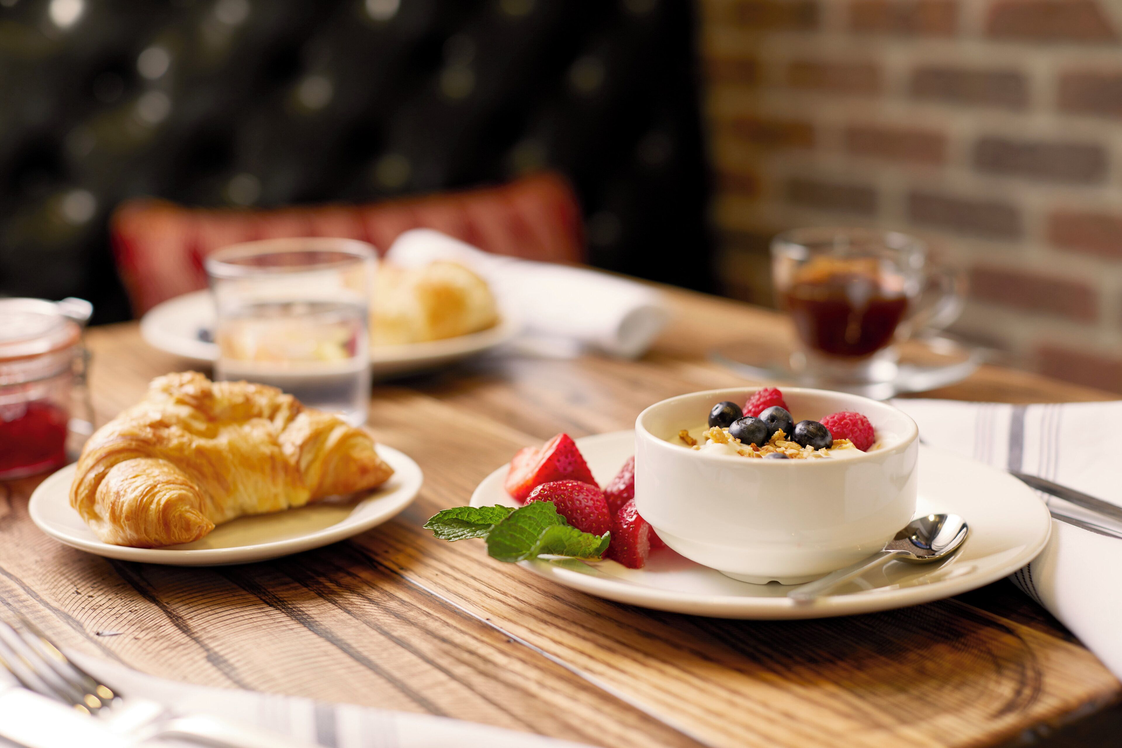 Disposição para o café da manhã com croissants, morangos, amoras e iogurte sobre uma mesa de madeira.