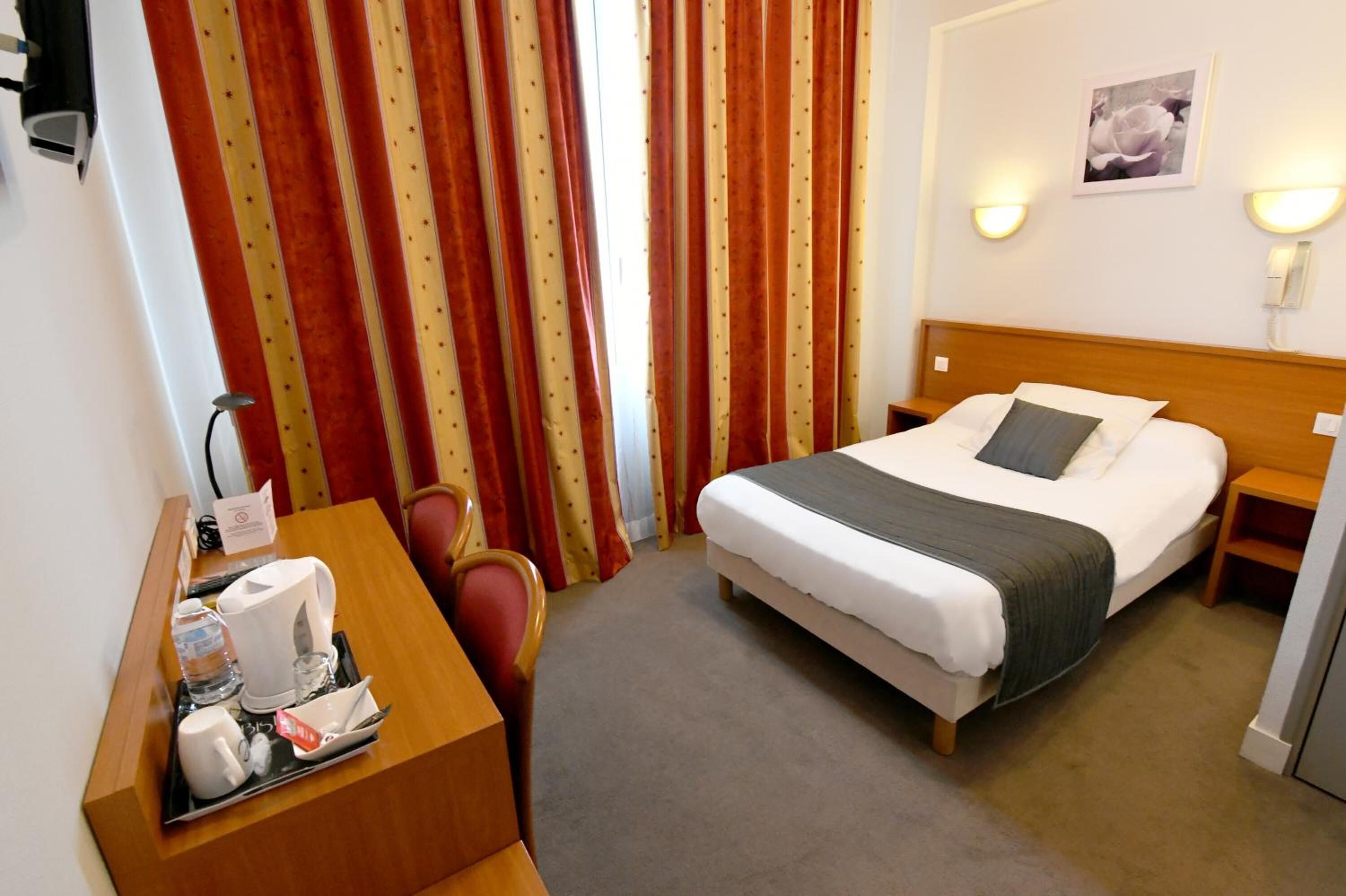 Quarto de hotel com cama, mesa de cabeceira, cadeira e cortinas.