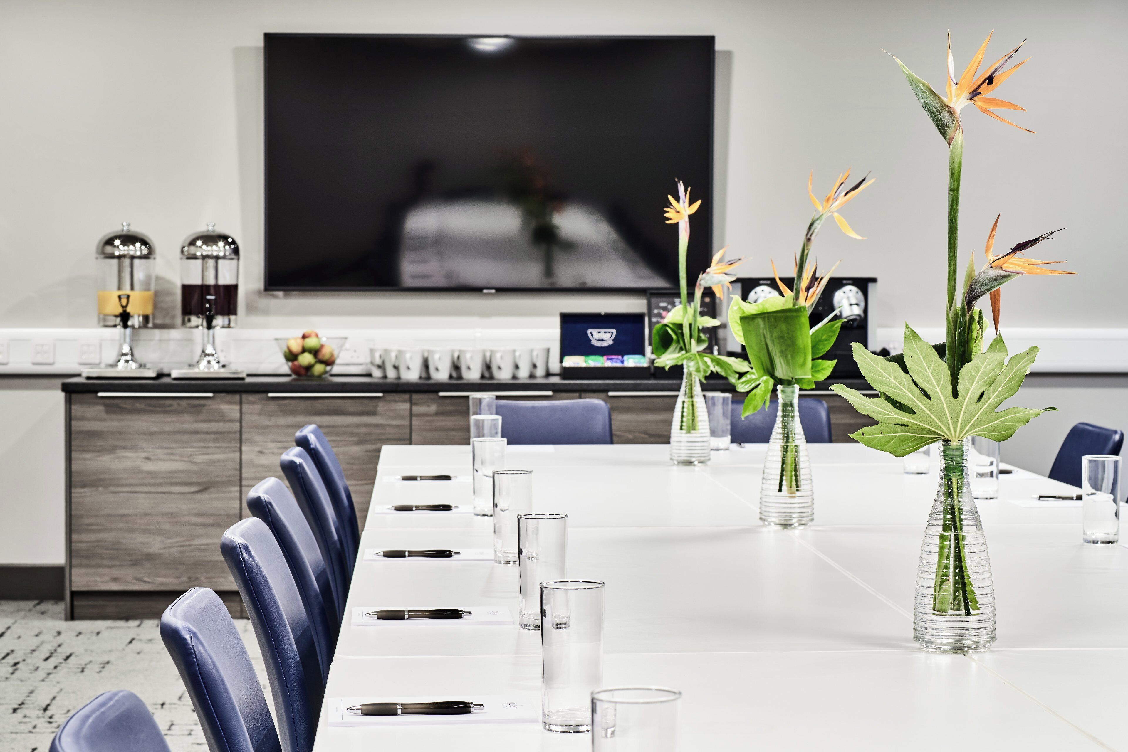 Uma sala de jantar moderna com uma mesa comprida, cadeiras e vasos com flores.