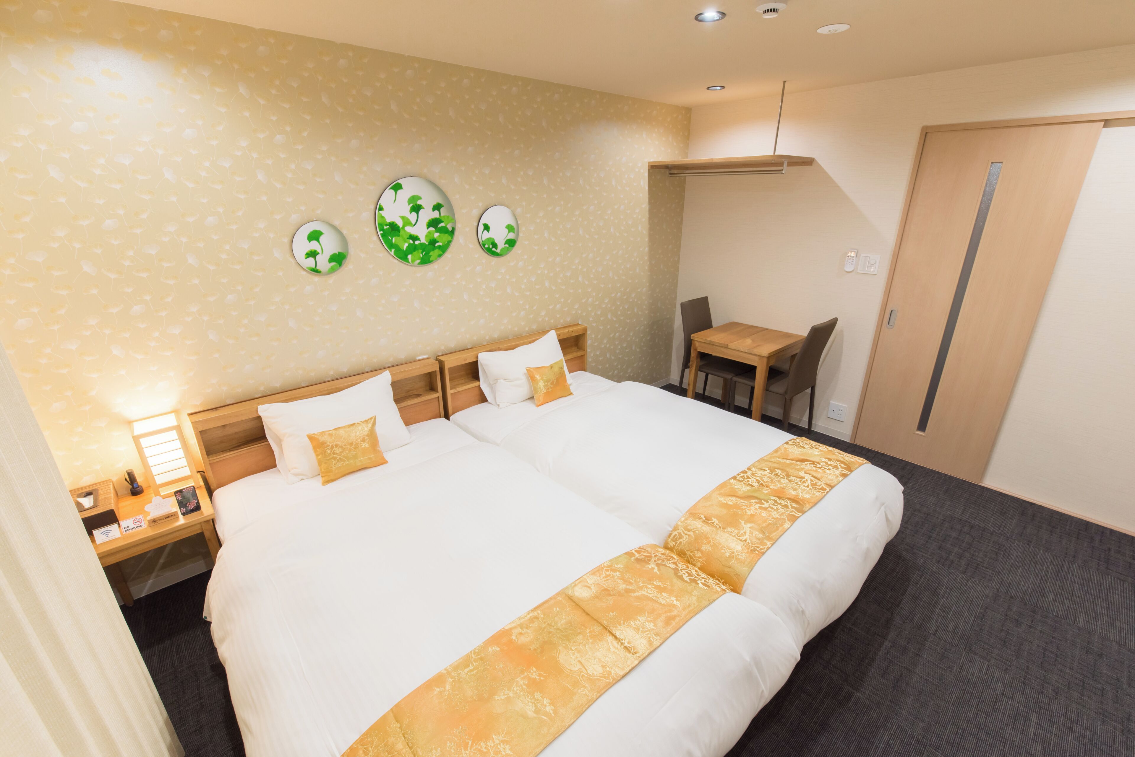 Quarto de hotel com uma cama grande, uma escrivaninha com cadeira, uma mesinha e uma porta.