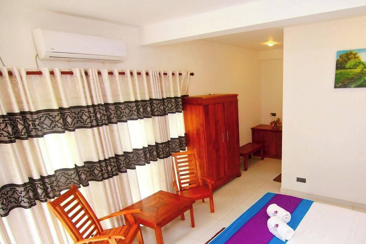 Quarto com uma cama, uma cadeira de madeira, uma mesinha, um armário, um ar condicionado e um quadro na parede.