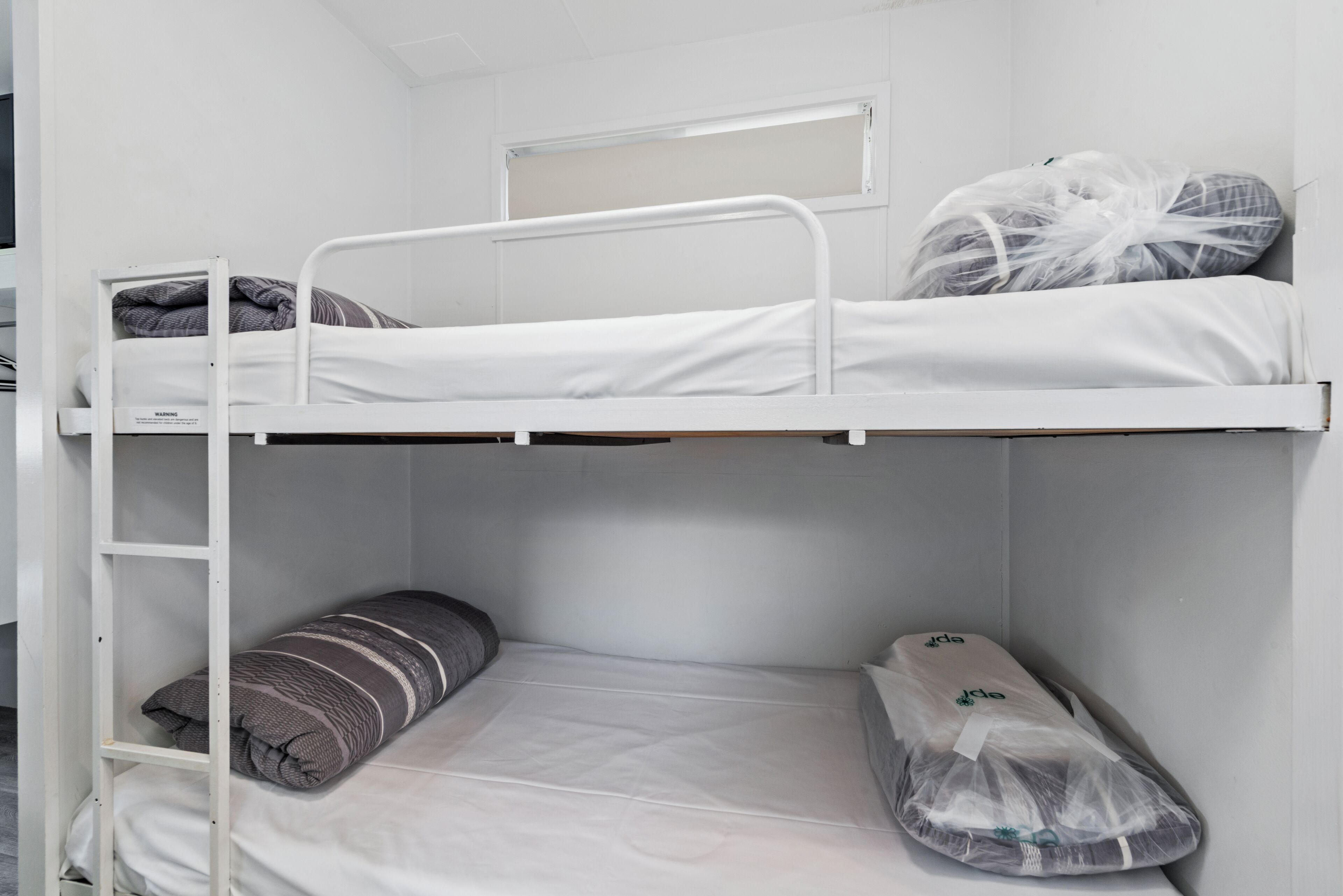 Uma cama beliche com escada, janela e uma pequena prateleira.