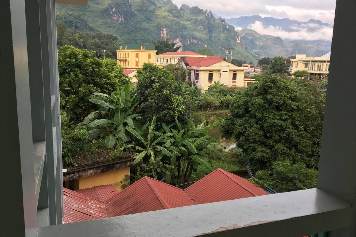 Vista de uma varanda com vista para uma área residencial, casas, vegetação exuberante e montanhas ao fundo.