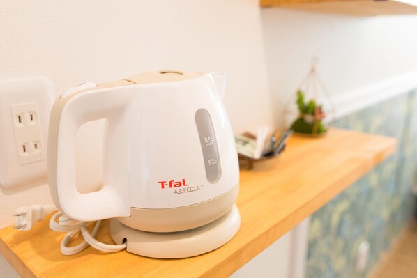 Uma chaleira elétrica branca da T-fal sobre uma bancada de madeira, com uma tomada elétrica ao fundo.
