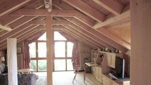 Um quarto de sótão espaçoso, com teto alto, vigas de madeira, uma janela grande, uma mesa de jantar e uma área de cozinha.