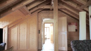 Interior em madeira com teto inclinado, porta visível para outro espaço e uma cadeira com padrão.