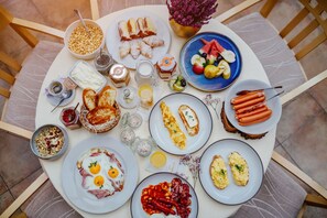 Mesa redonda com diversos itens de café da manhã, incluindo ovos, salsichas e frutas.