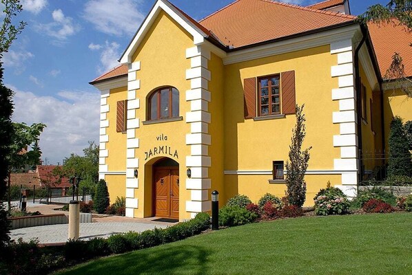 Um edifício amarelo com o nome "Villa Jarmila" na fachada, apresentando um estilo arquitetônico tradicional com telhado de telhas e entrada central.