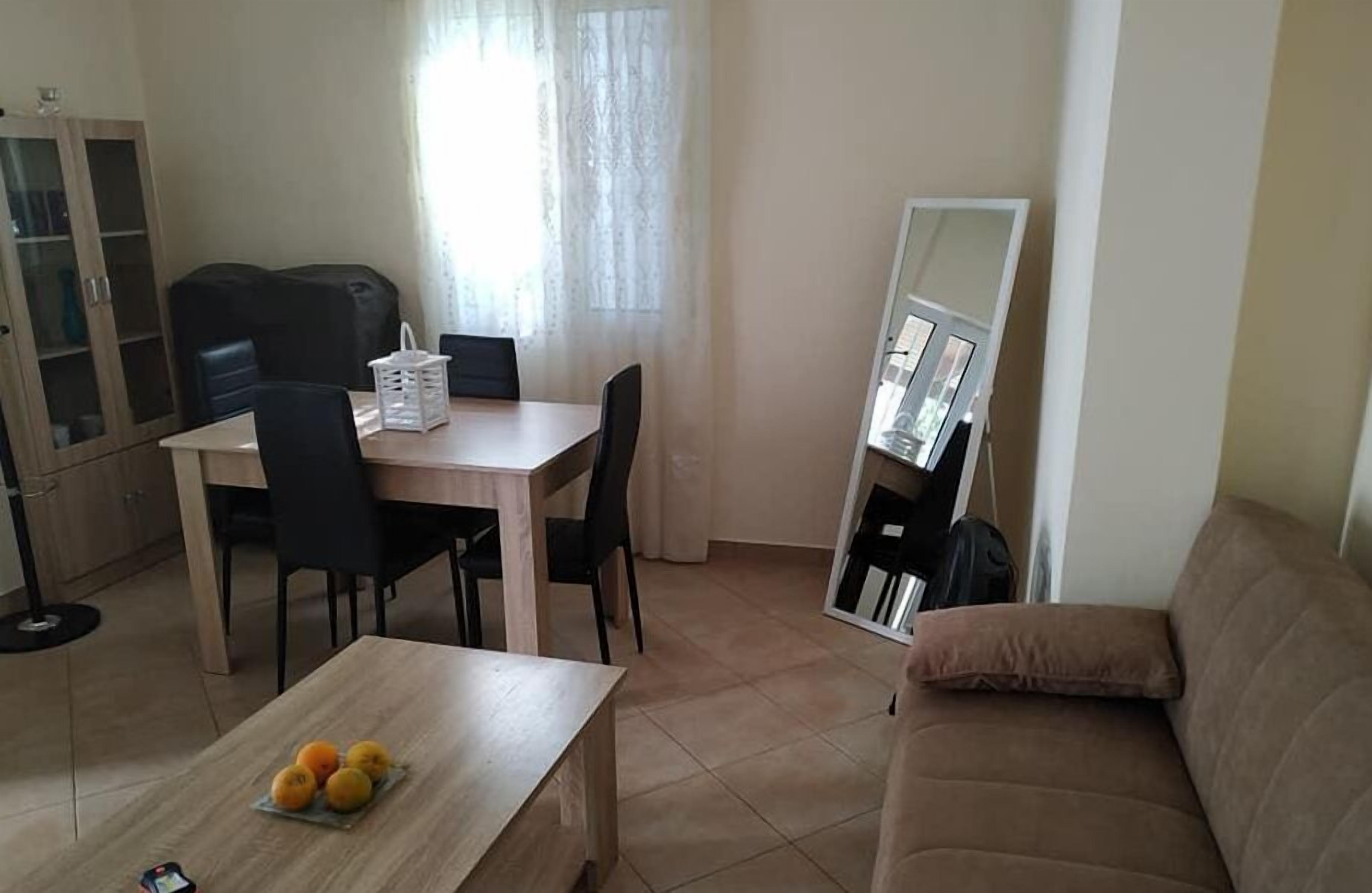 Uma sala de estar com uma mesa de madeira, duas cadeiras pretas, um sofá marrom, um armário e um espelho.