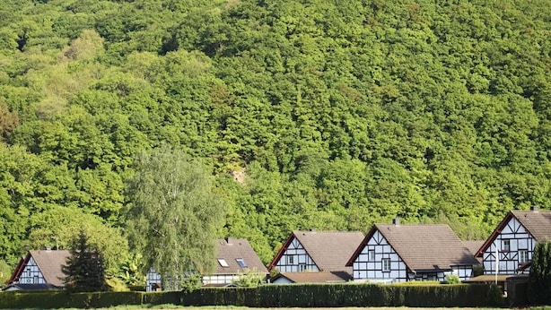 Uma fileira de casas tradicionais de enxaimel com uma colina arborizada ao fundo.