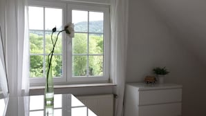 Quarto com uma janela grande, penteadeira branca e uma pequena planta sobre ela.
