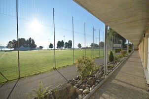 Um campo esportivo com uma cobertura de passagem e um edifício ao fundo.