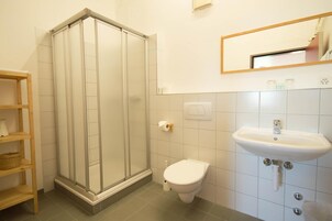 Casa de banho com cabine de duche, sanita, lavatório e espelho sobre o lavatório.