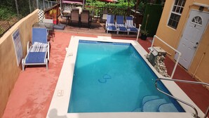 Piscina retangular com placa indicando 3 pés de profundidade, rodeada por espreguiçadeiras e uma área de deck com mesas e cadeiras.