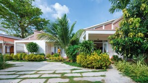 Um imóvel residencial com calçada pavimentada, vegetação exuberante e uma casa de dois andares com varanda.