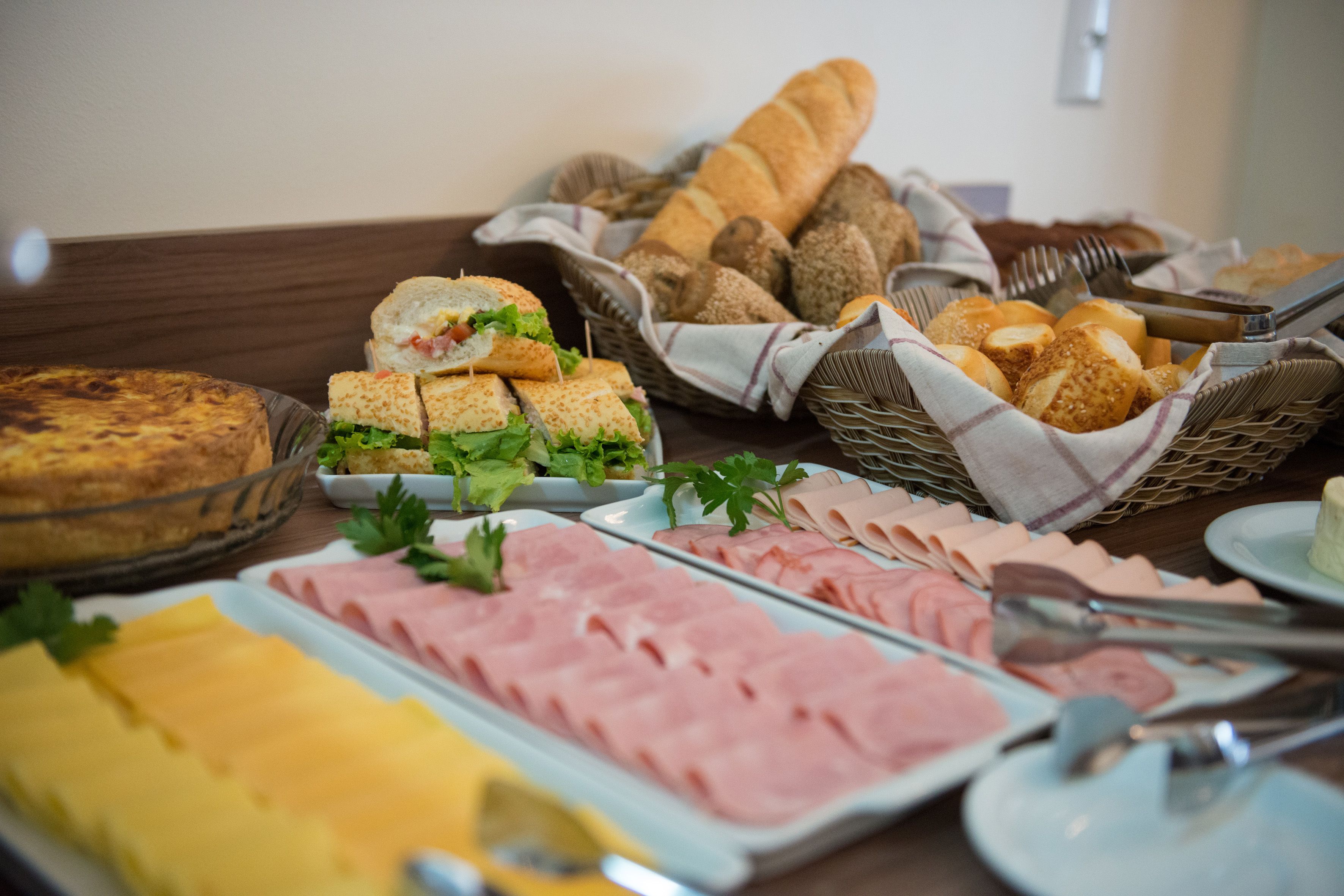 Buffet com diversas opções de comida, incluindo sanduíches, pães e frios fatiados.
