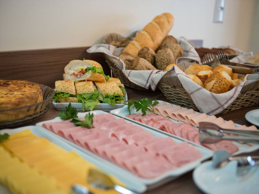Buffet com diversas opções de comida, incluindo sanduíches, pães e frios fatiados.