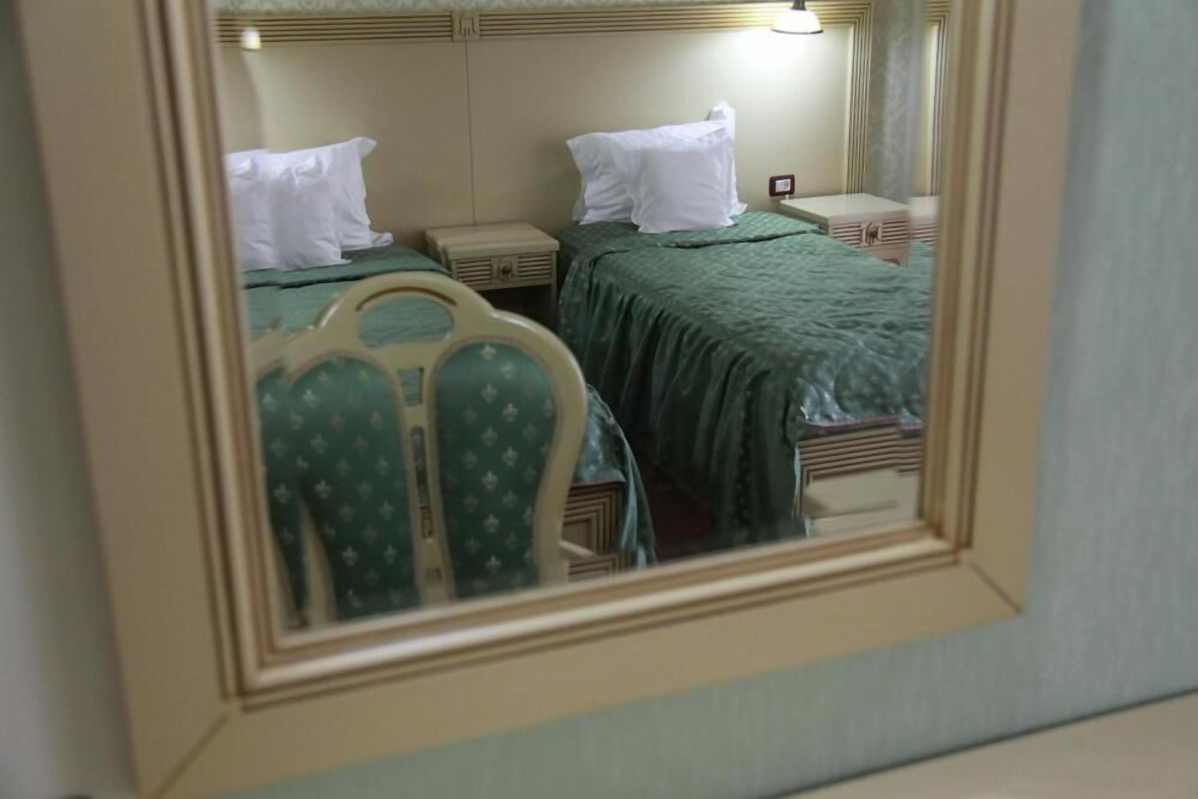 Quarto com duas camas, cada uma com colcha verde e almofadas brancas. Pequena mesa de cabeceira com abajur em cada cama.