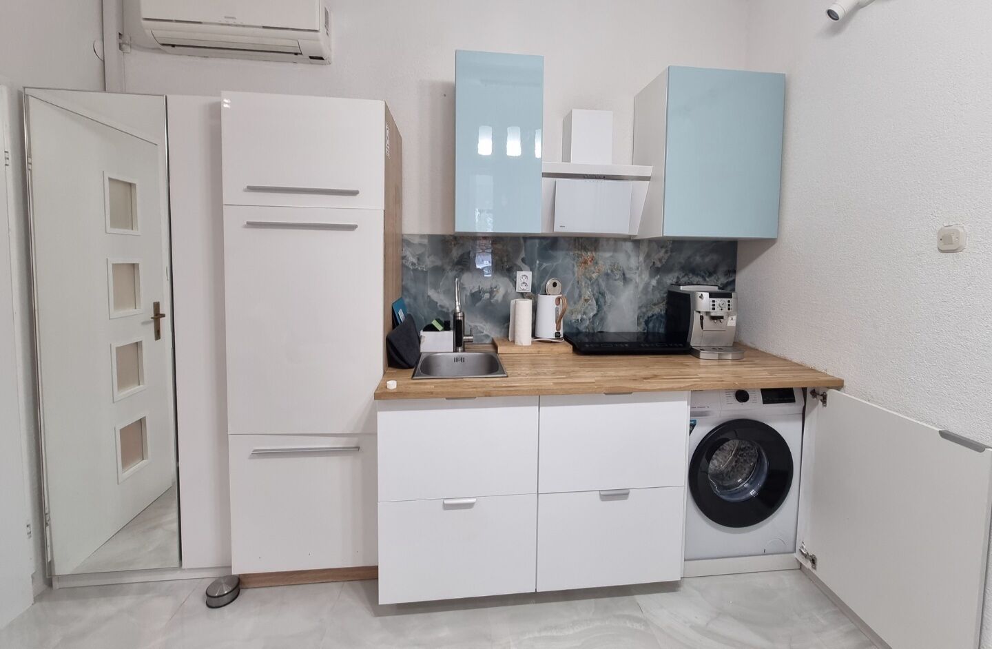 Uma cozinha compacta com máquina de lavar, geladeira e micro-ondas.