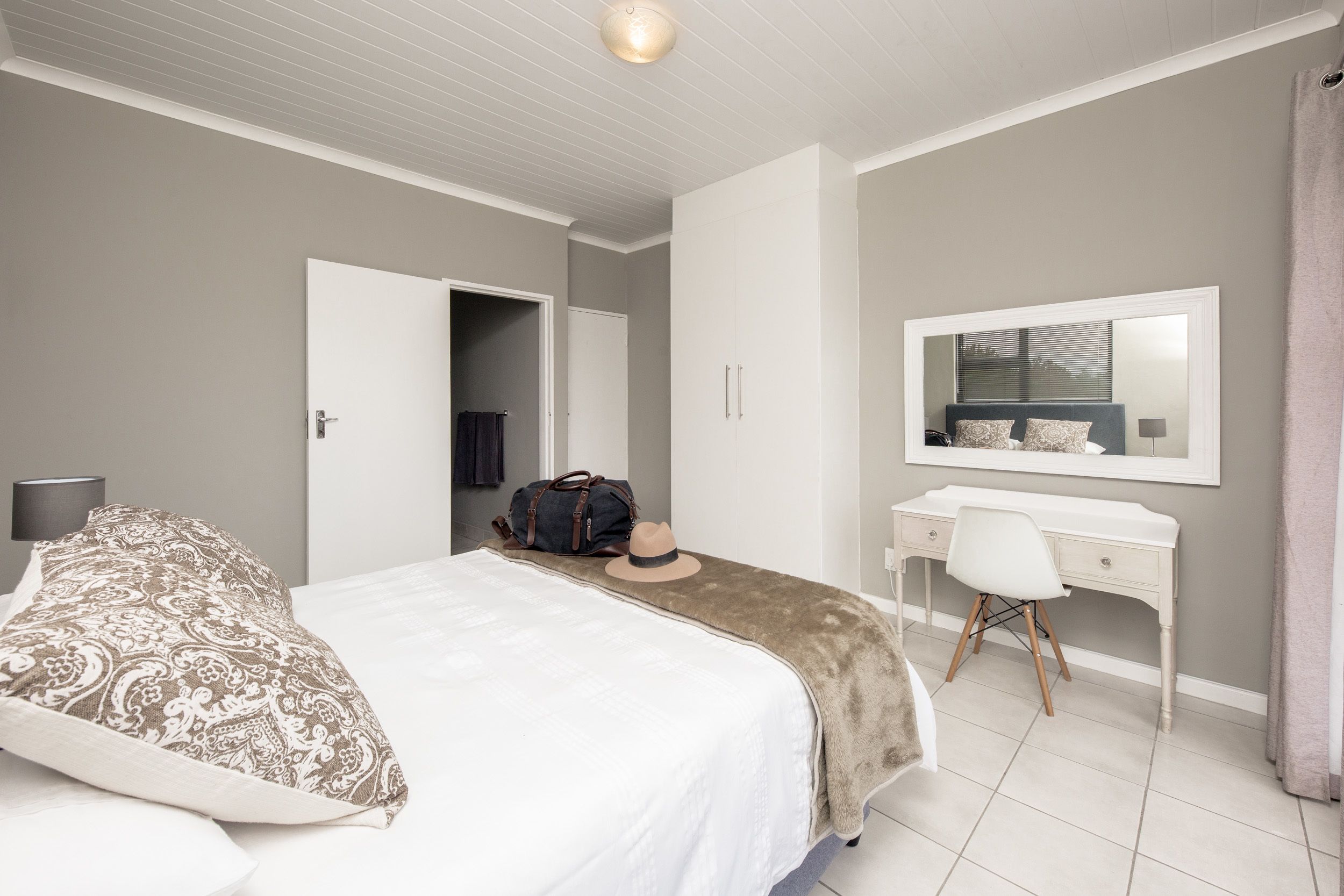 Um quarto com cama, escrivaninha, guarda-roupa e espelho.
