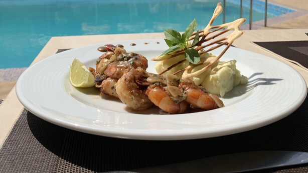 Uma mesa de jantar com um prato de comida, uma piscina e um edifício ao fundo.