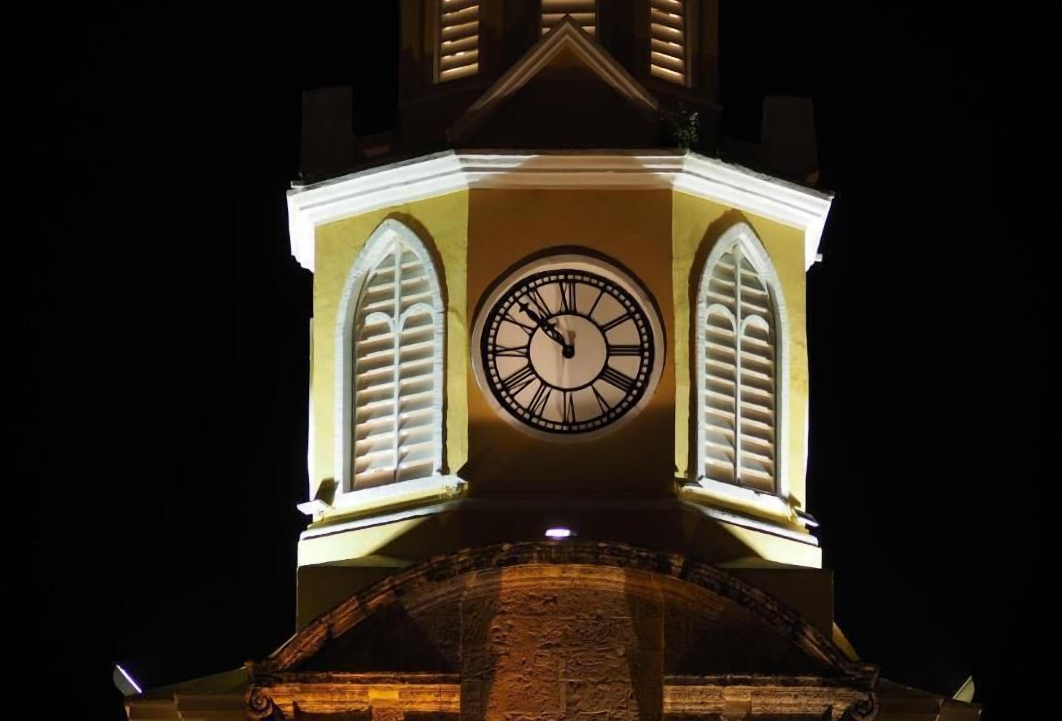 Um campanário com um grande mostrador de relógio iluminado e duas janelas em arco.