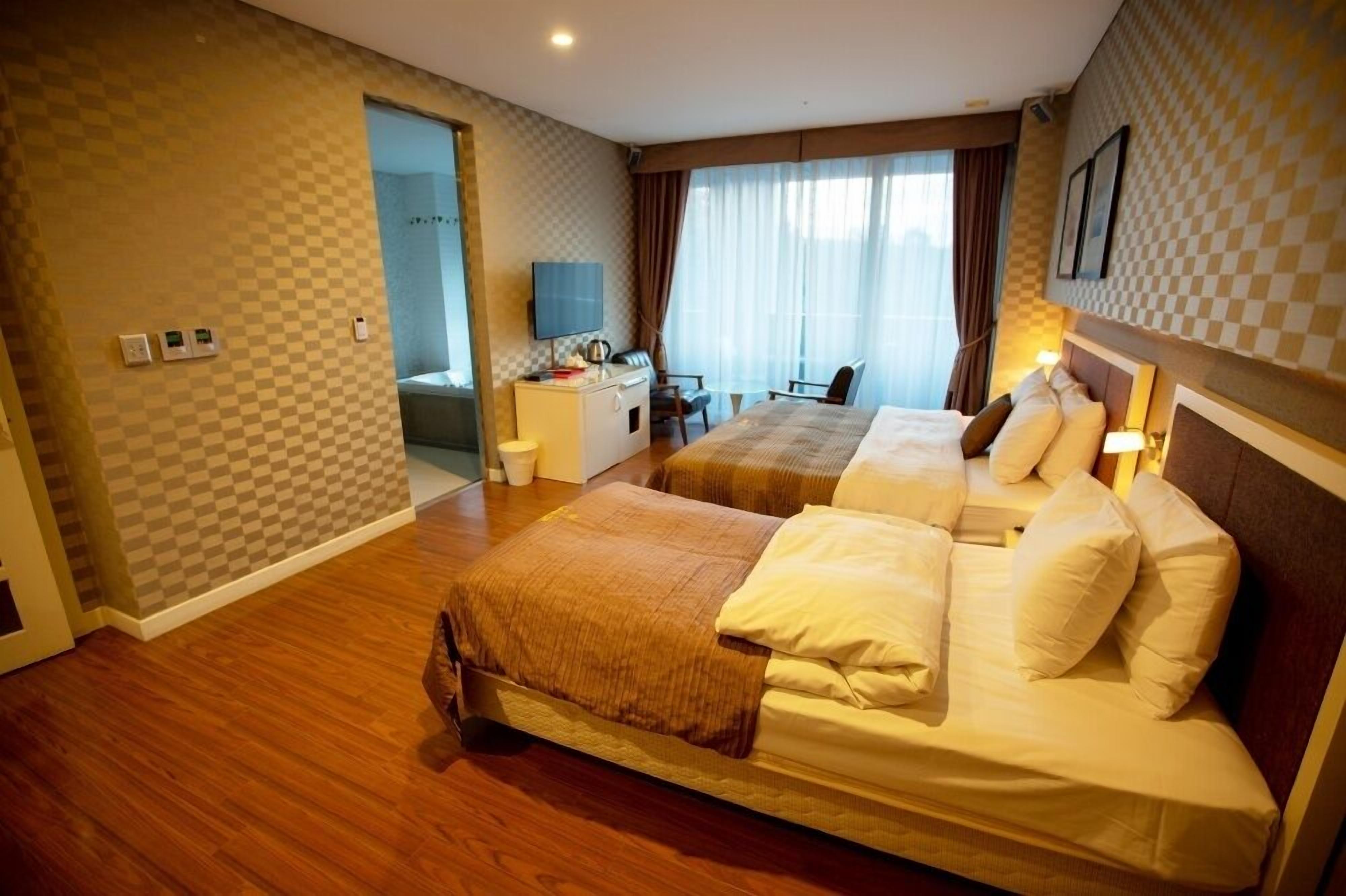 Quarto de hotel com duas camas, uma escrivaninha, uma cadeira e uma televisão.