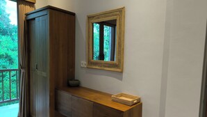 Um armário de madeira com um espelho acima, uma pequena cesta sobre o armário e vista para o verde lá fora.