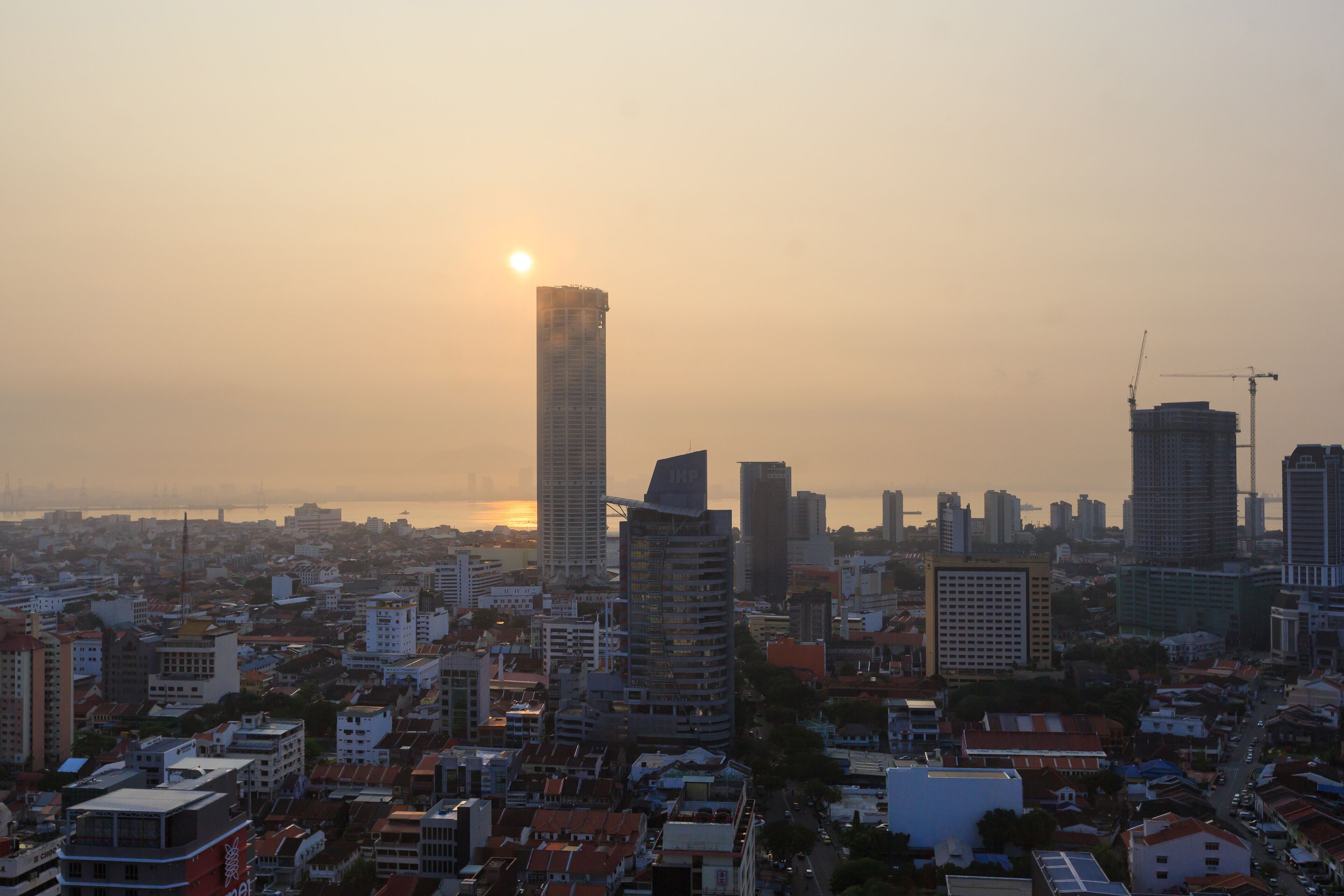 Paisagem urbana com um edifício alto imponente, diversos outros edifícios altos e um corpo de água ao fundo.