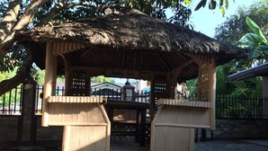 Um gazebo de madeira com telhado de palha, um banco e uma placa com a inscrição 'Bubble Side'.