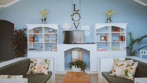Sala de estar com dois sofás, uma mesa de centro, lareira e estantes brancas com livros e objetos decorativos.