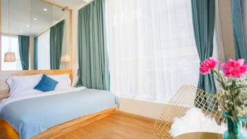 Quarto com cama, espelho, janela com cortinas, cadeira e vaso com flores.
