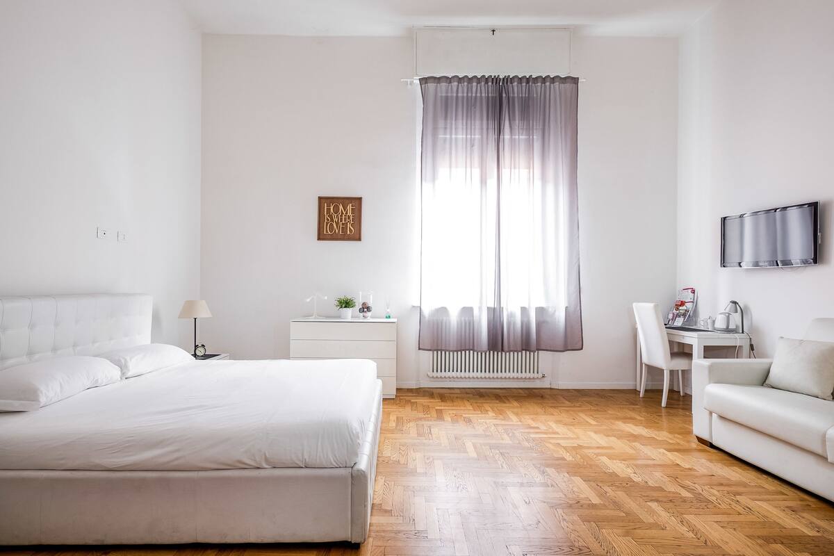 Quarto moderno com cama grande, escrivaninha, cadeira e televisão.